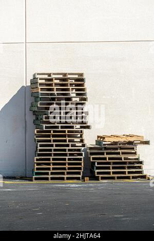 Empty wooden pallets stacked outdoors on concrete sidewalk beside metal ...