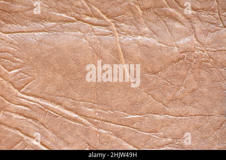A fragment of natural brown leather with wrinkles, folds and small dark ...