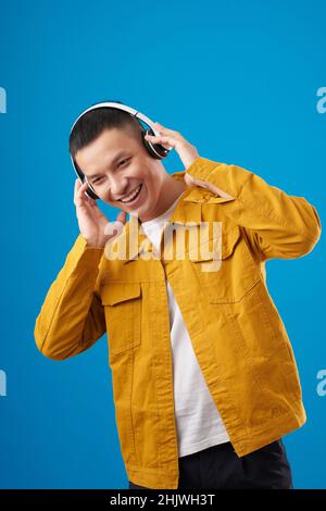 Joyful man in headphones dancing and using mobile phone isolated over ...