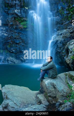 young man at waterfall falling streams from mountain top with ...
