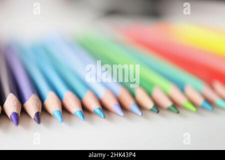 Many sharp multicolored pencils lying over colors of rainbow closeup ...