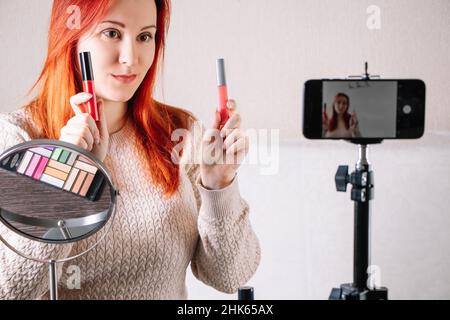 Young redhead woman recording make up tutorial with smartphone at home ...