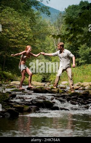 Young couple helping each other over stream Stock Photo - Alamy