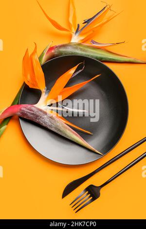 Simple table setting with bird of paradise flower on orange background ...