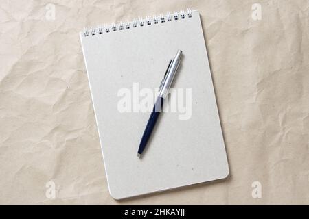 Gray notepad with white coiled spring and pen on a background of beige ...