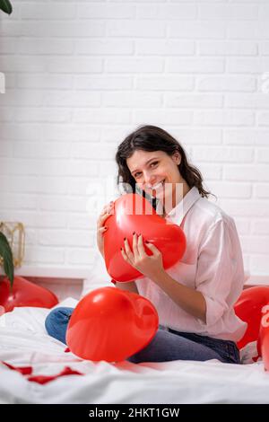 Brunette European girl rejoices playing on bed with red heart shape ...