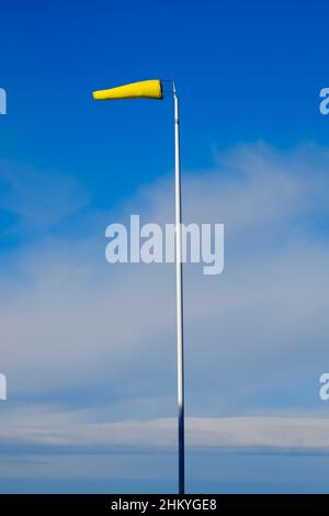 Yellow windsock on a pole against a blue sky with light clouds. Showing ...