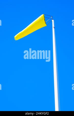 Yellow windsock on a pole against a blue sky with light clouds. Showing ...
