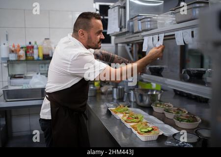 Chef taking order slip in commercial kitchen. Caucasian chef reads out ...