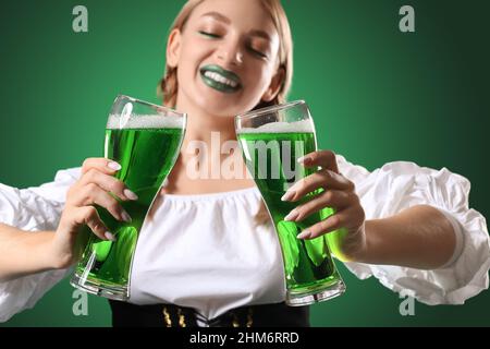 Beautiful Irish waitress with glasses of beer on green background. St ...