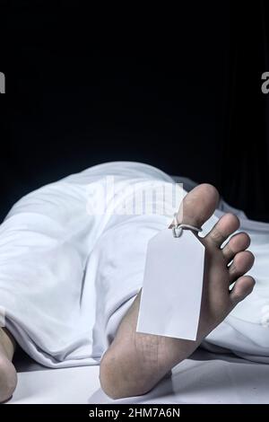 Human corpse covered with a sheet and name tag on toe in the morgue ...