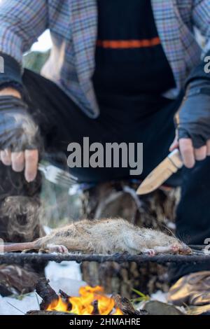 The homeless man grills a rat, in a snowy landscape, close up view ...