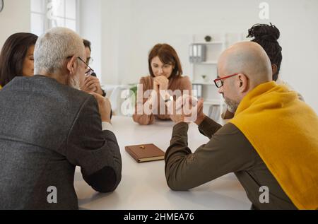 Diverse group of people praying to Lord sitting together around table ...