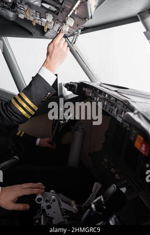 cropped view of pilot reaching control panel near co-pilot using yoke ...