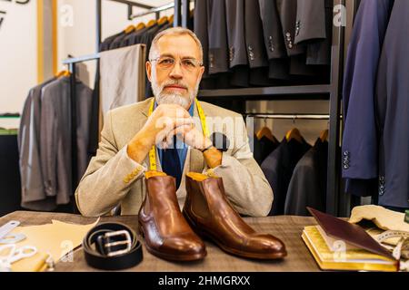 An elderly shoemaker showing handmade male shoes and belt in a workshop ...