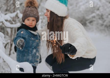 Mom and son are walking and light sparklers in the snow winter forest ...