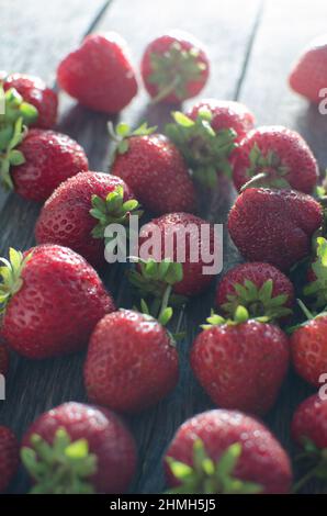 Ripe red strawberries controlam bright light on the old wooden table ...