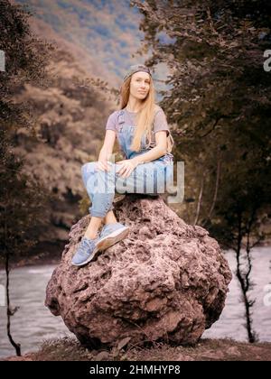 A fair-haired woman in denim casual outfit sits on the street steps ...