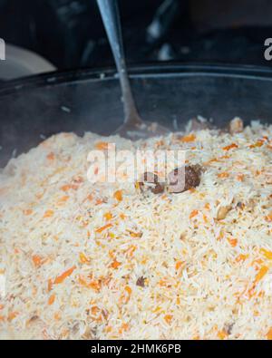 Cooking Uzbek pilav of rice and, carrot and meat in metal pan outside ...