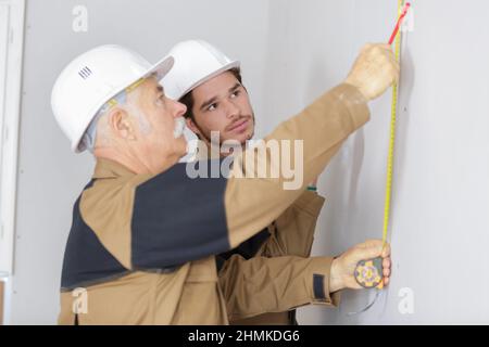 builder apprentice and senior workmen measuring wall Stock Photo - Alamy