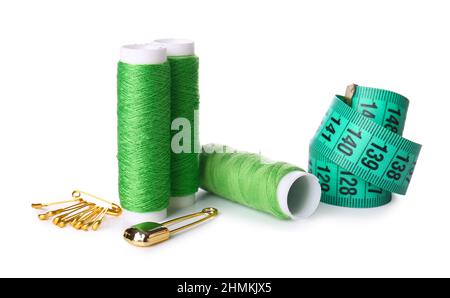 Green thread spools, safety pins and ball pins on white background ...