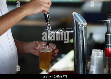 Bartender pouring beer from faucet machine in to big plastic glass ...