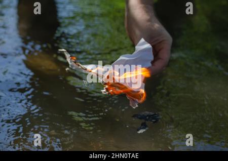 A mature man holds a burning piece of paper in his hand. Crumpled white ...