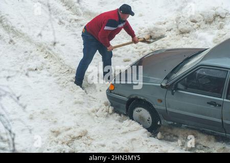 A man digs a shovel of snow from a car stuck in the snow Stock Photo ...