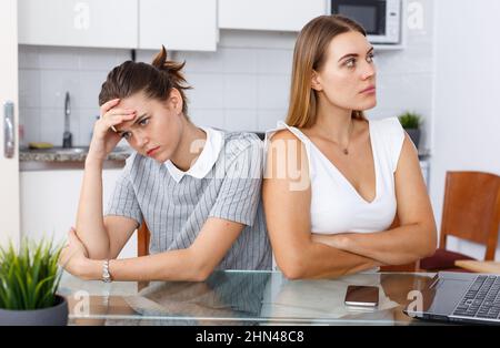 Two angry friends after a quarrel sitting on a couch and looking at the ...