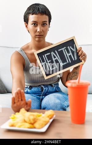 Young hispanic woman rejecting fast food holding healthy blackboard at ...