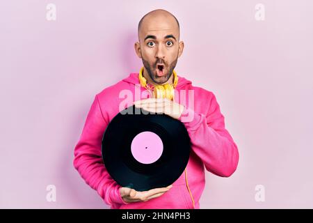 Young hispanic man holding vinyl disc covering mouth with hand, shocked ...