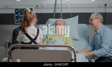 Niece and daughter visiting sick grandma in hospital ward bed, bringing ...