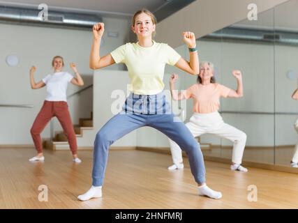 Teen girl with family exercising dance moves with group of people in ...