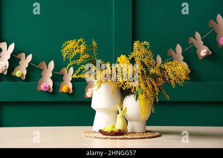 Vases with mimosa flowers, Easter eggs and decor on dining table near ...