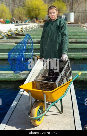 Portrait of female worker of sturgeon farm standing near fish tank ...