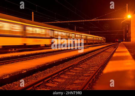 White and blue train passing a small roofless train station at night in ...