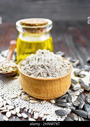 Sunflower flour in bowl, oil in glass jar, seeds in a spoon on burlap ...