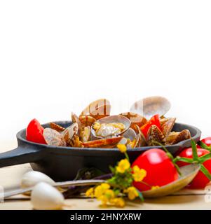 fresh clams stewed on an iron skillet over wite rustic wood table Stock ...