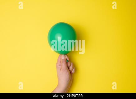 Female hand holding an inflated green air balloon on a yellow ...