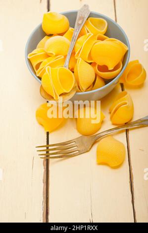 Raw Italian snail lumaconi pasta on a blue bowl over rustic table macro ...