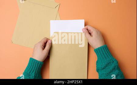 female hand holds paper envelopes on an orange background, top view ...