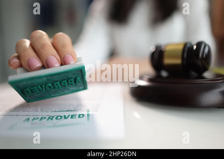 Hand puts stamp approved on document near judge's gavel Stock Photo - Alamy