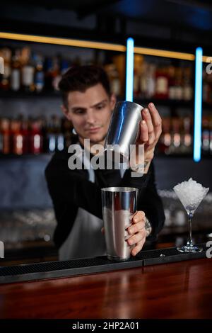 Handsome barman making elegant cocktail in night club on bar counter ...