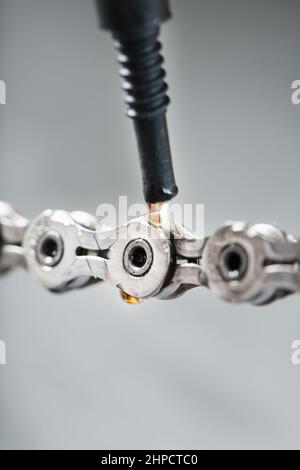Greasing a bicycle chain with a drop of golden oil close-up on a gray ...