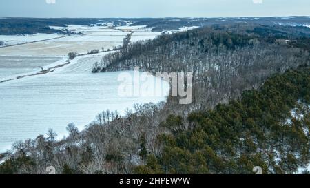 Snow covers the hills and fields with farm fields between the slopes ...