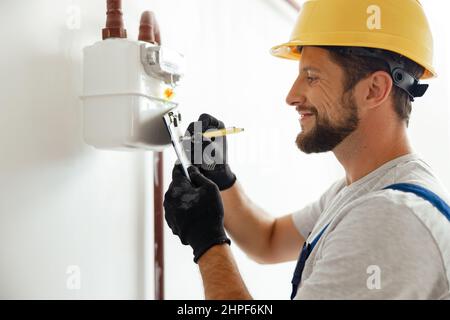 Happy professional heating fitter making notes while checking gas ...