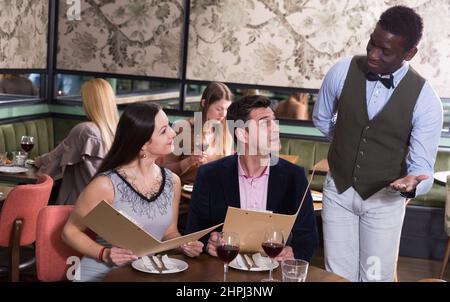 African American waiter recommending dishes from restaurant menu Stock ...