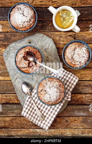 A cup of tea, a spoon, two chocolate cakes on a plate and a sheet of ...