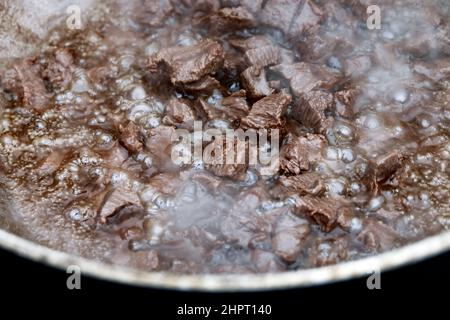 Pieces of meat for pilaf are stewed in cauldron over bonfire Stock ...