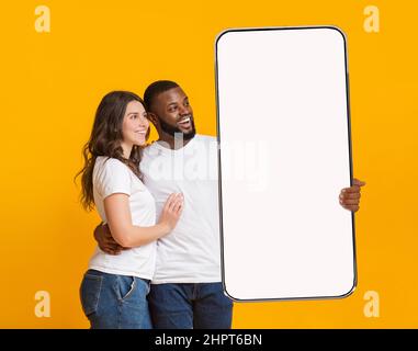 Interracial couple showing blank empty smartphone screen for mockup ...